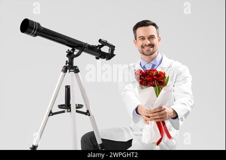 Happy male astronomer with bouquet of tulips, greeting card and ...