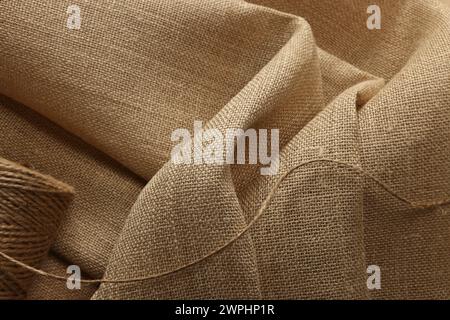 Spool of thread and burlap fabric on wooden table, top view. Space for ...