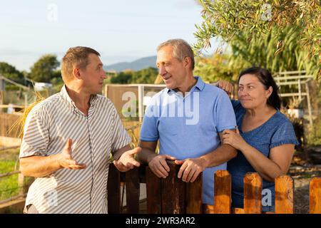 Three neighbours farmers talking together near wooden fence in garden ...