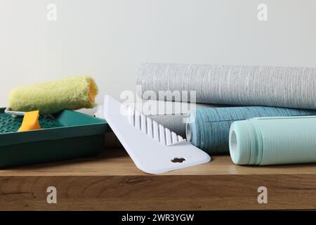Different wallpaper rolls, roller and plastic spatula on wooden table ...