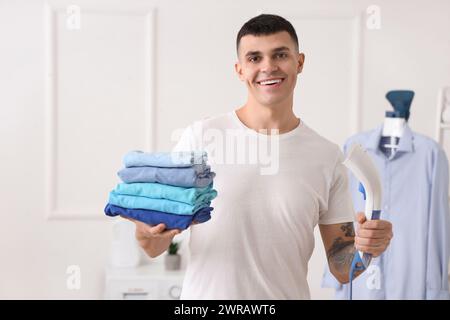 Happy young man with steamer and stack of clean clothes on orange ...