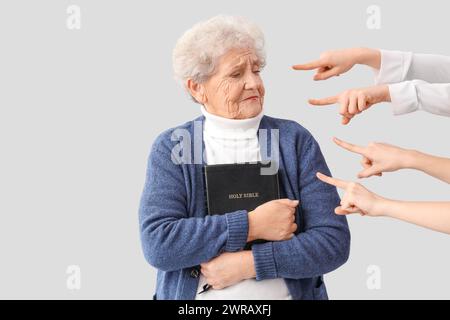 People pointing at senior woman with Holy Bible on green background ...