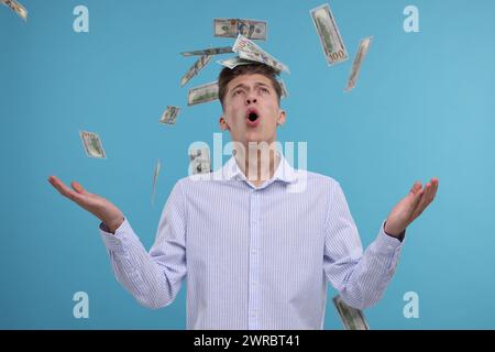 Excited man under money shower on light blue background. Abbreviation ...