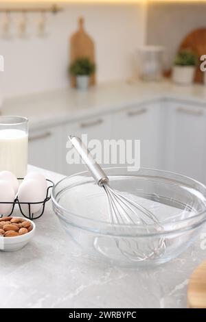 Metal whisk, bowl and different products on gray marble table in ...