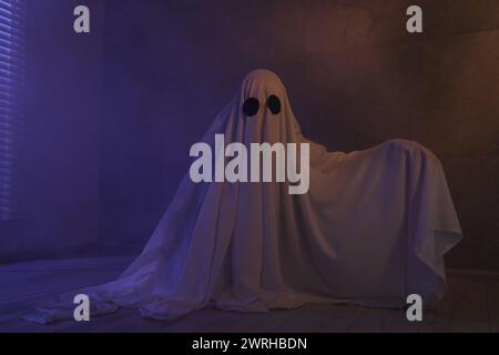Creepy ghost. Woman covered with sheet near window in color lights ...