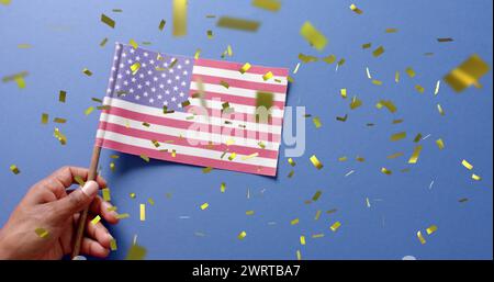 Image of confetti falling over hand holding flag of united states of ...