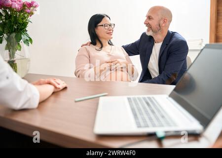 Adult husband and his pregnant wife visiting gynecologist office for routine health check-up of ...