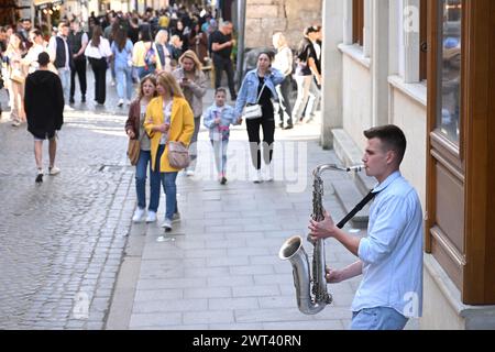 A street musician performs as people walk past, against the backdrop of ...