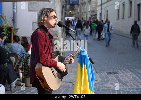 A street musician performs as people walk past, against the backdrop of ...