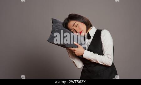 Asian front desk staff falling asleep with pillow in hand, feeling ...