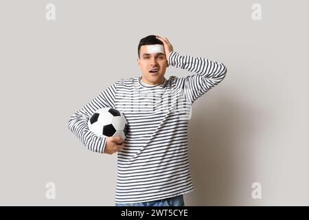Young man with brain concussion and soccer ball on light background ...