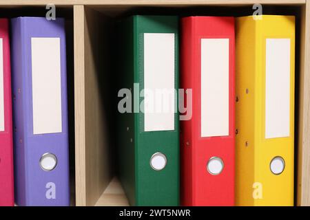 Colorful binder office folders on shelving unit near light grey wall ...