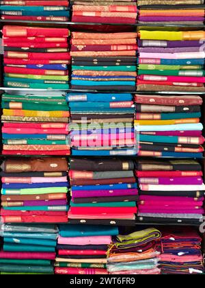 Neatly stacked colorful designer silk saris in racks in a textile shop ...
