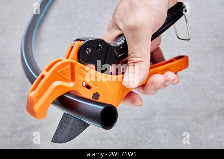 Orange ratcheting PVC pipe cutter tool in hand of plumber cutting off ...