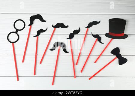 Fake paper mustaches and bow tie party props on white wooden background ...