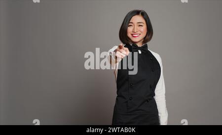 Asian waitress pointing at camera to choose you over grey background ...
