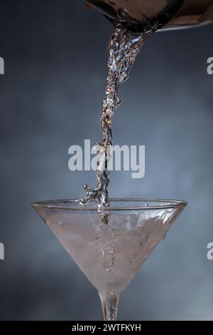 Action shot of pouring chilled gin into a martini glass over a blueish background Stock Photo ...