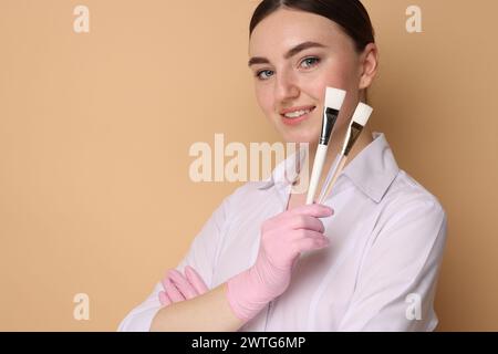 Cosmetologist with cosmetic brushes on beige background, space for text ...