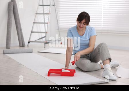 Woman applying glue onto wallpaper sheet in room Stock Photo - Alamy