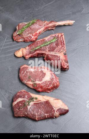 Fresh raw beef cuts with herbs on light grey textured table, flat lay ...