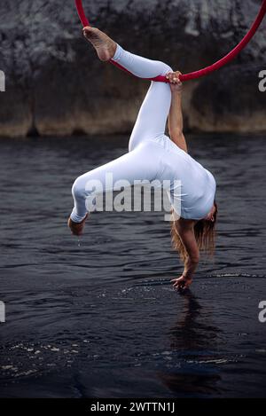 Athletic woman performing an aerial acrobatics split using red fabric ...