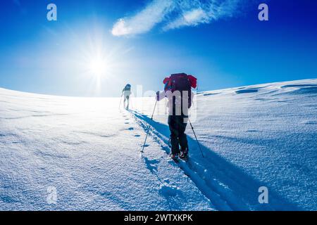 a ski tourer climbing uphill towards a bright sun in the mountains of ...