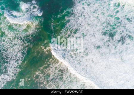 An aerial drone view of foamy waves crashing on a white sandy beach on ...