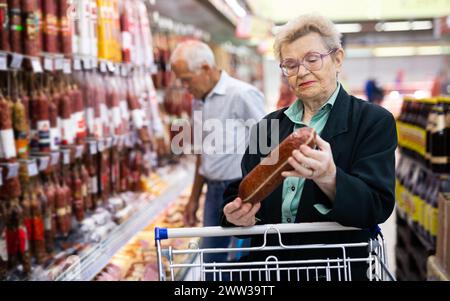 mature woman with glasses picks out salami in the meat section of the ...