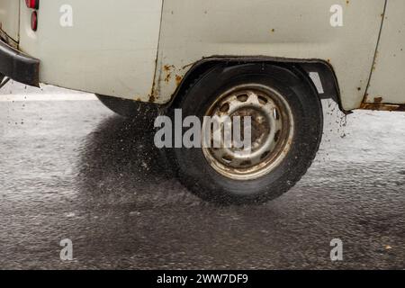 old rusty soviet minivan driving on the wet asphalt road during heavy ...