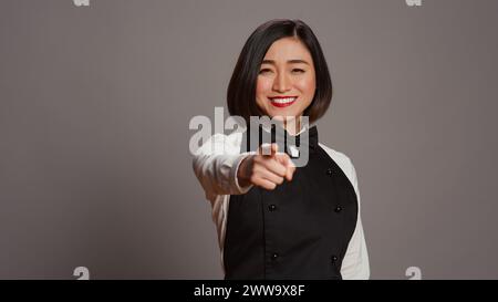 Asian waitress pointing at camera to choose you over grey background ...
