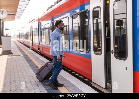 Happy man with suitcase entering into the train and waving on station ...