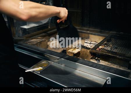 Partial male chef frying fish fillet and vegetables in burning fire ...
