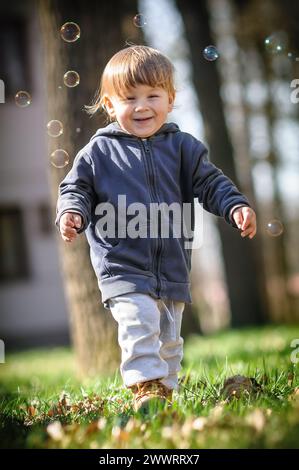 Happy smiling cute toddler delights in chasing floating soap bubbles ...