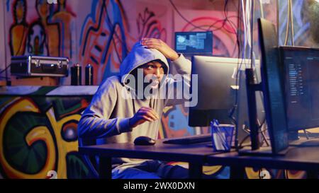 Hacker in graffiti painted hideaway base writing lines of code on ...