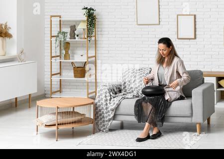 Beautiful mature woman with sticks playing glucophone on sofa at home ...