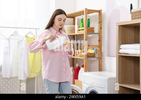 Beautiful young woman pouring detergent into cap in laundry room Stock ...