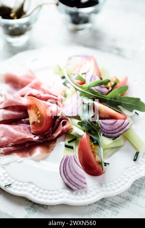 Plate of smoked ham with tomatoes and rocket. Bright wooden background ...