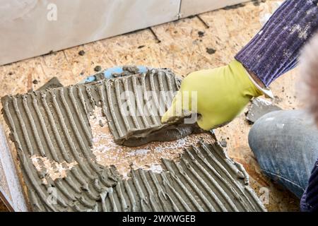 Construction worker applying adhesive mortar on a tile surface using a ...