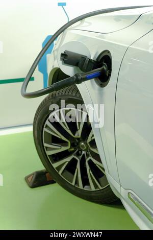 White electric car connected to the grid at a charging station in a ...