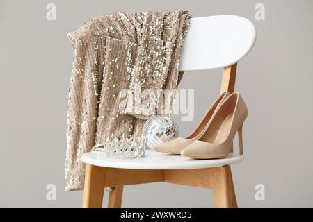 Prom dress, shoes, crown and disco ball on chair against grey ...