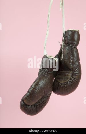 a pair of old boxing gloves hung in front of a candy-pink background ...