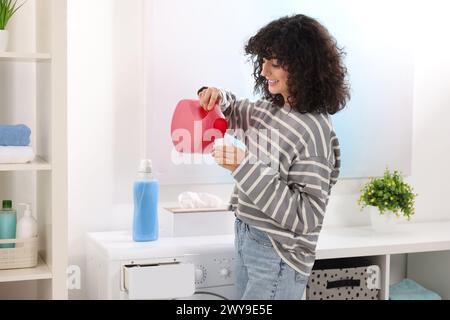 Woman pouring detergent into cap near washing machine indoors, closeup. Laundry day. Space for ...