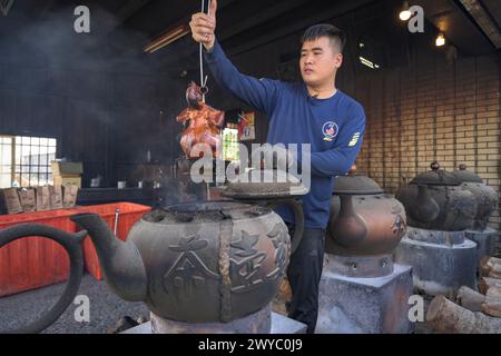 A man cooking a chicken using traditional clay pots over a wood fire ...