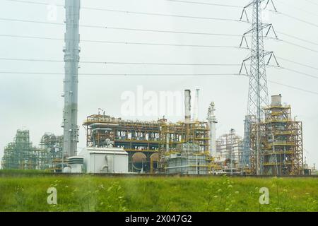 An oil refinery stands tall in the middle of a vast field, with pipes ...