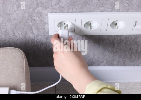 Woman plugging power bank into socket on grey wall indoors, closeup ...