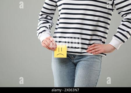 Woman holding sticky note with drawn sad face and suffering from ...