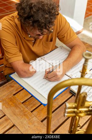 A one-armed male trumpeter in a home courtyard engrossed in writing ...