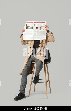 Male spy with newspaper sitting on bag against light background Stock ...