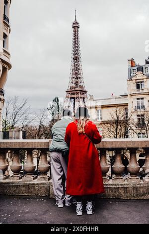 Couple looking at the Eiffel Tower from a street in Paris. Woman in red ...