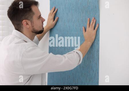 Man hanging light blue wallpaper in room Stock Photo - Alamy